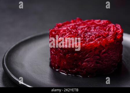 Cooked grated beetroot formed as a cylinder and ready dish on a black ...