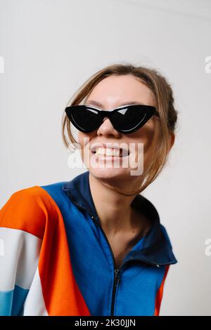 A smiling woman wearing white sunglasses and a white shirt stands in ...