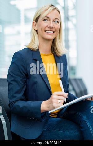 Smiling businesswoman with tablet PC and digitized pen talking to ...
