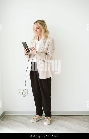 Woman using mobile phone while charging electric car at charging ...