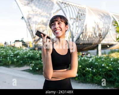 young, cheerful woman talking on smartphone while standing at kitchen ...