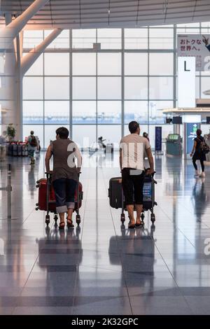 Travelers push trolleys of luggage at Haneda International Airport ...