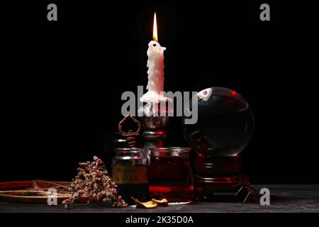 Burning candle, jars with potion and crystal ball on dark background ...