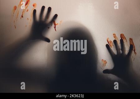 Horror ghost woman with blooded hands behind the matte glass. Halloween ...