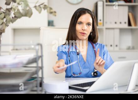 Woman physician giving recipe, sitting at table in office Stock Photo ...