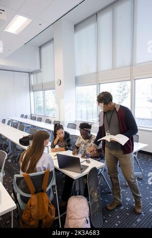 Four students talking and discussing with their professor in the ...