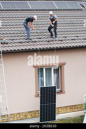 Technicians lifting up solar panel on metal beams for installing. Male ...