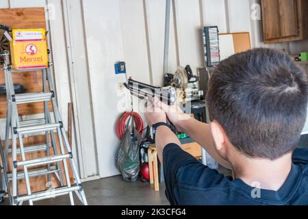 Over the shoulder view of a boy aiming and shooting an air pistol in a ...