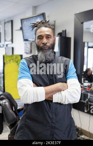 Portrait of confident mature male barber in apron with beard standing ...