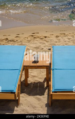 Closeup view of two blue sunbeds and a small table in front of the ...