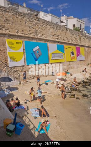 Local people and tourists at a beach by the old town of Monopoli ...