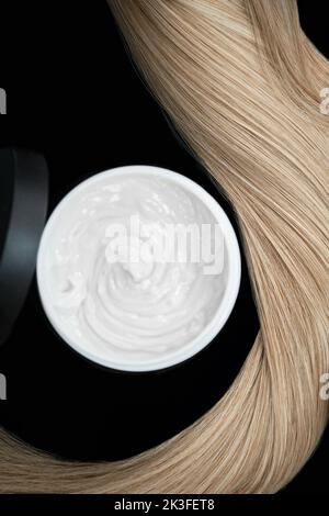A strand of blond hair with hair balm on a black background. Close-up ...