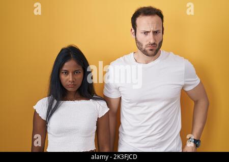 Interracial couple standing over yellow background doing peace symbol ...