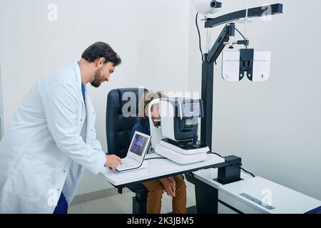 Optometrist using autorefractor check patient vision. Eye exam of adult ...