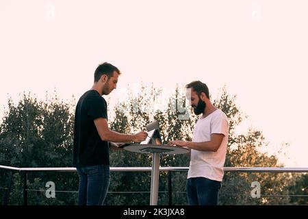 Two young entrepreneur men having a business talk while working online ...