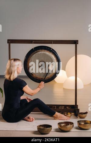 A woman knocks a mallet with a hammer on a gong. A gong and a hand ...