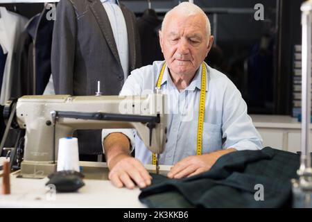 Portrait of elderly tailor working on sewing machine at studio Stock ...