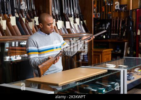 Portrait of male standing with rare collectible rifle in hunting shop ...