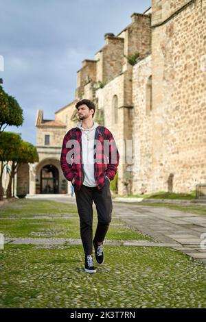 Full body of serious male traveler strolling on street along medieval ...
