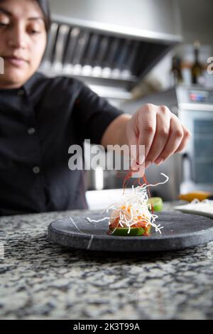 Hispanic female chef putting white daikon on lime slice placed on ...