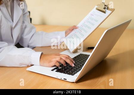 Anonymous ethnic female medic writing on netbook during video chat at ...