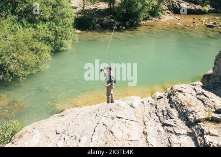 From above male fisherman throwing fishing rod into a mountain river ...