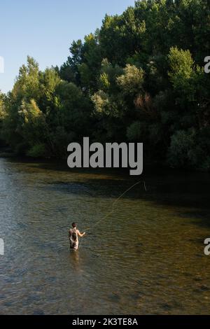 From above male fisherman throwing fishing rod into a mountain river ...