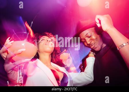 Drunk African American couple dancing under bright neon light while ...