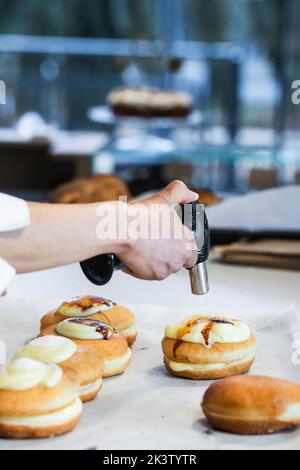 Unrecognizable crop chef caramelizing sugar cream on sweet Berliners ...