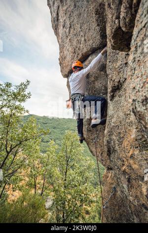 Male mountaineer climbing high cliff with safety carabiner and ropes ...