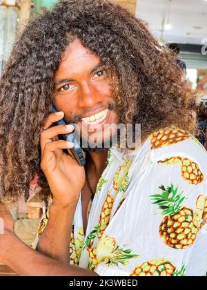 Portrait of cheerful young black guy at railway station reading text ...