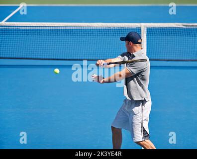 Showing up to every tennis practice. Rearview shot of a man about to ...