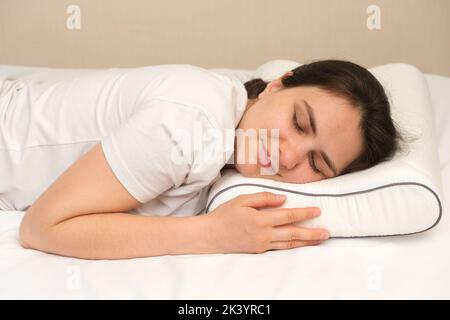 A woman sleeps on her stomach on an orthopedic pillow made of memory ...
