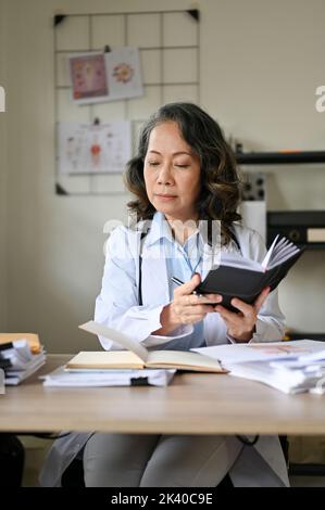 Asian woman doctor reading book resting on couch with laptop computer ...
