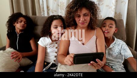 Brazilian mother and children staring at cellphone screen together at ...