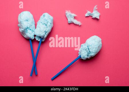 Horizontal image of homemade blue candy floss on three sticks, on pink ...