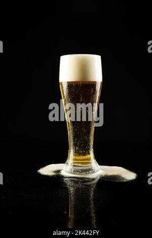Image of overflowing pint glass of foamy beer, with copy space on black ...