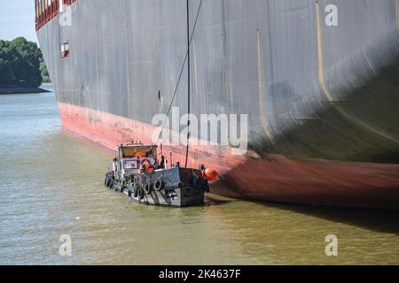 Tanker boat or bunker barge at the hull of a large container freighter ...