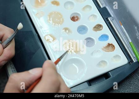 Dental technician adds glaze and shading to a set of fake teeth, at the ...