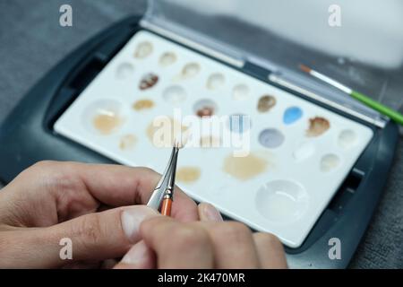 Dental technician adds glaze and shading to a set of fake teeth, at the ...