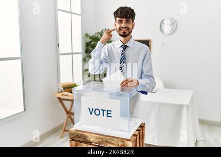 Hispanic man with beard voting putting envelop in ballot box doing ...