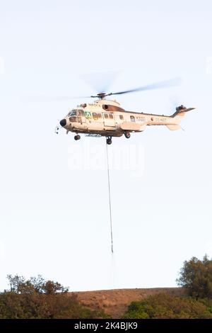 A White Airbus Helicopters H215 refilling a water bucket as it works ...