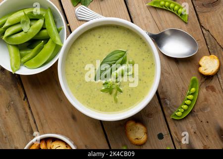 Horizontal image of bowl of pea soup, with peas and basil leaves on ...