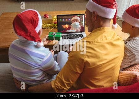 Caucasian father and sons in santa hats making christmas laptop video ...