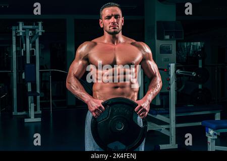 Powerlifter with weight disk in sport gym. Bodybuilder with heavy disk ...