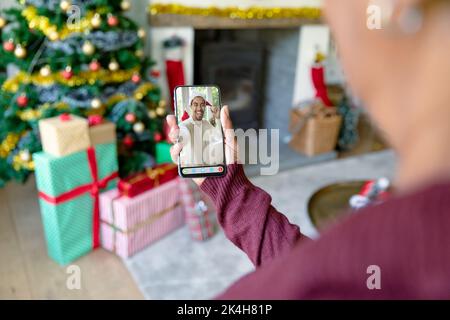 Woman making smartphone christmas video call with santa claus in face ...