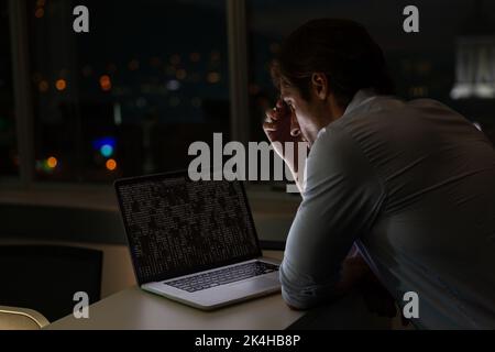 Caucasian male programmer sitting at desk, drinking coffee, using ...