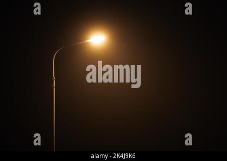 One night lamppost shines with faint mysterious yellow light through ...