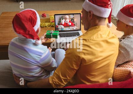 Father and sons in santa hats making laptop christmas video call with ...