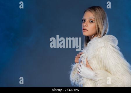 pierced woman with winter makeup and frozen eyebrows posing on dark ...